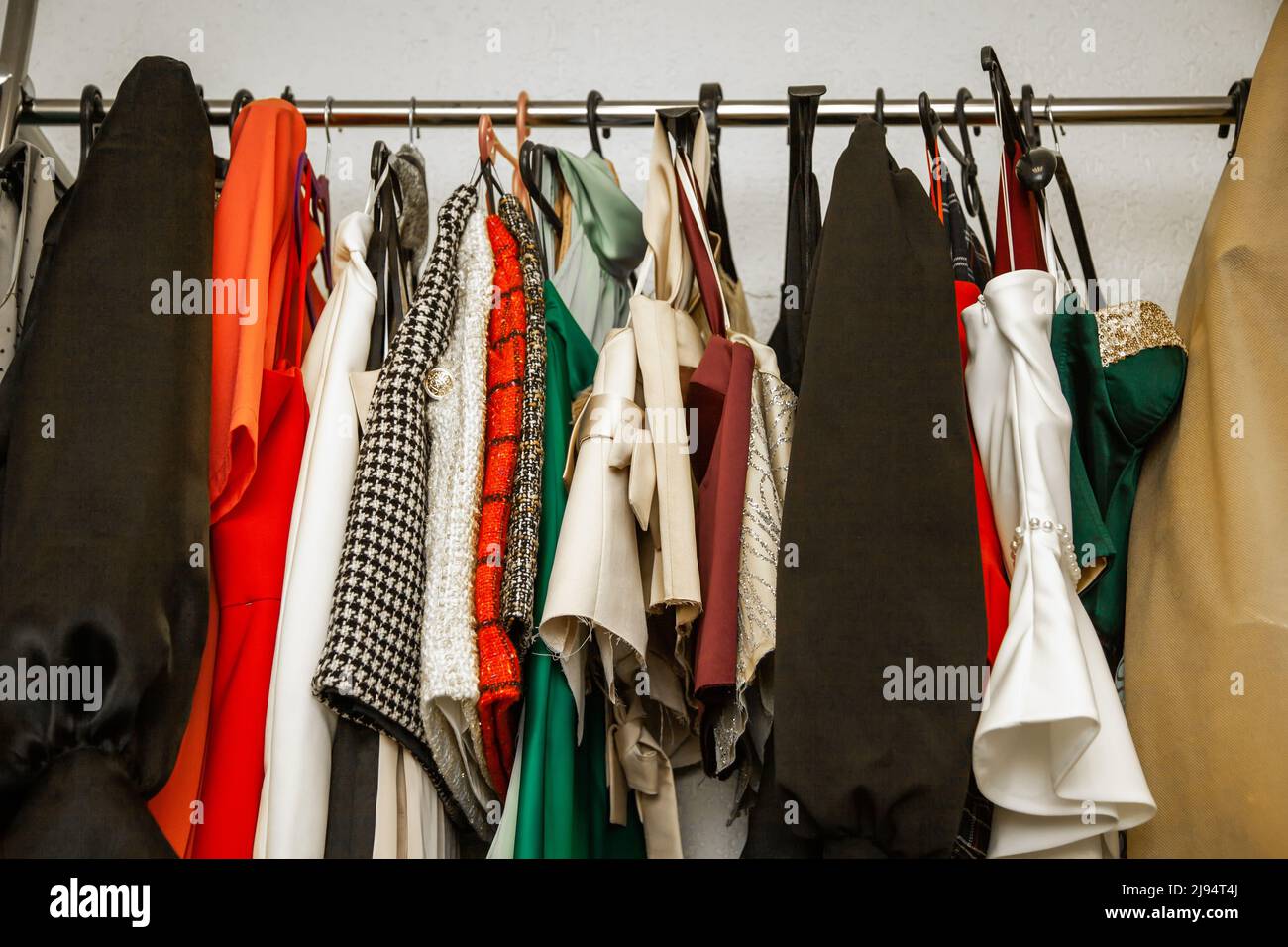 Rack with unfinished fashionable tailored clothes in atelier close up ...