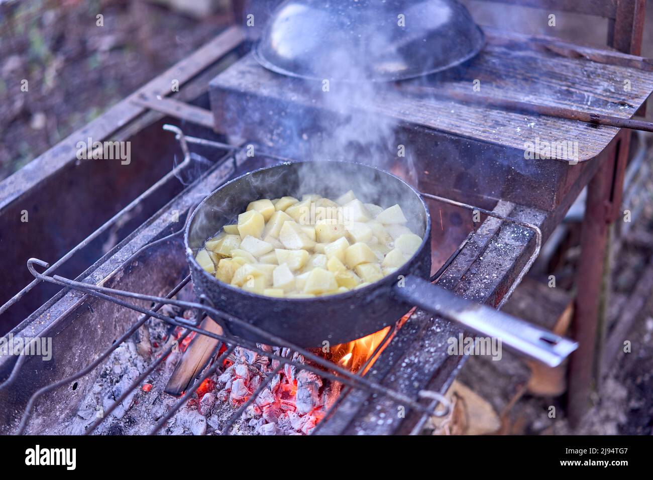 Fried potatoes on an open fire. The old frying pan is on the rack under ...