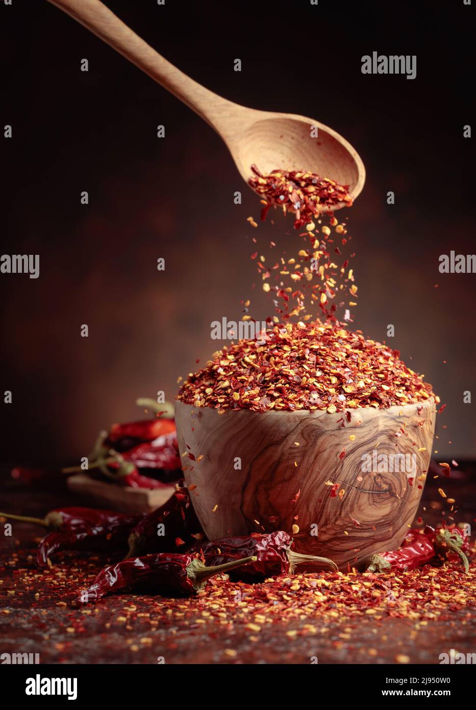 Chilli flakes are poured into a wooden dish. Chilli flakes and dried ...