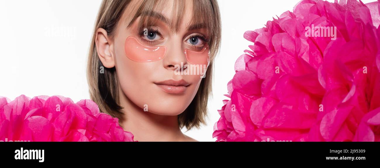 young woman with hydrogel eye patches near bright pink flowers isolated ...