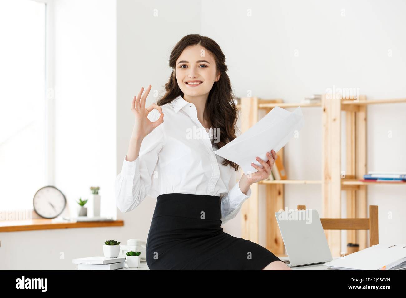 Businesswoman in formal wear holding documents and showing ok sign at ...