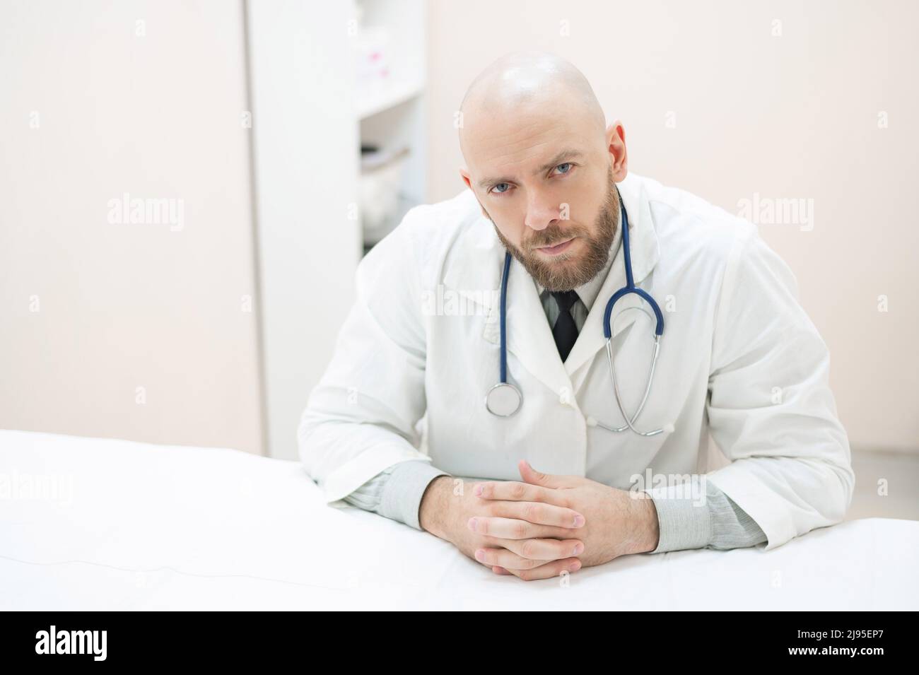 A male doctor sits at a desk in a medical office. A bald man with a ...