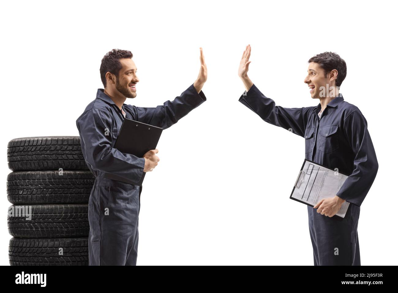 Two mechanic workers gesturing high five next to a pile of tires ...