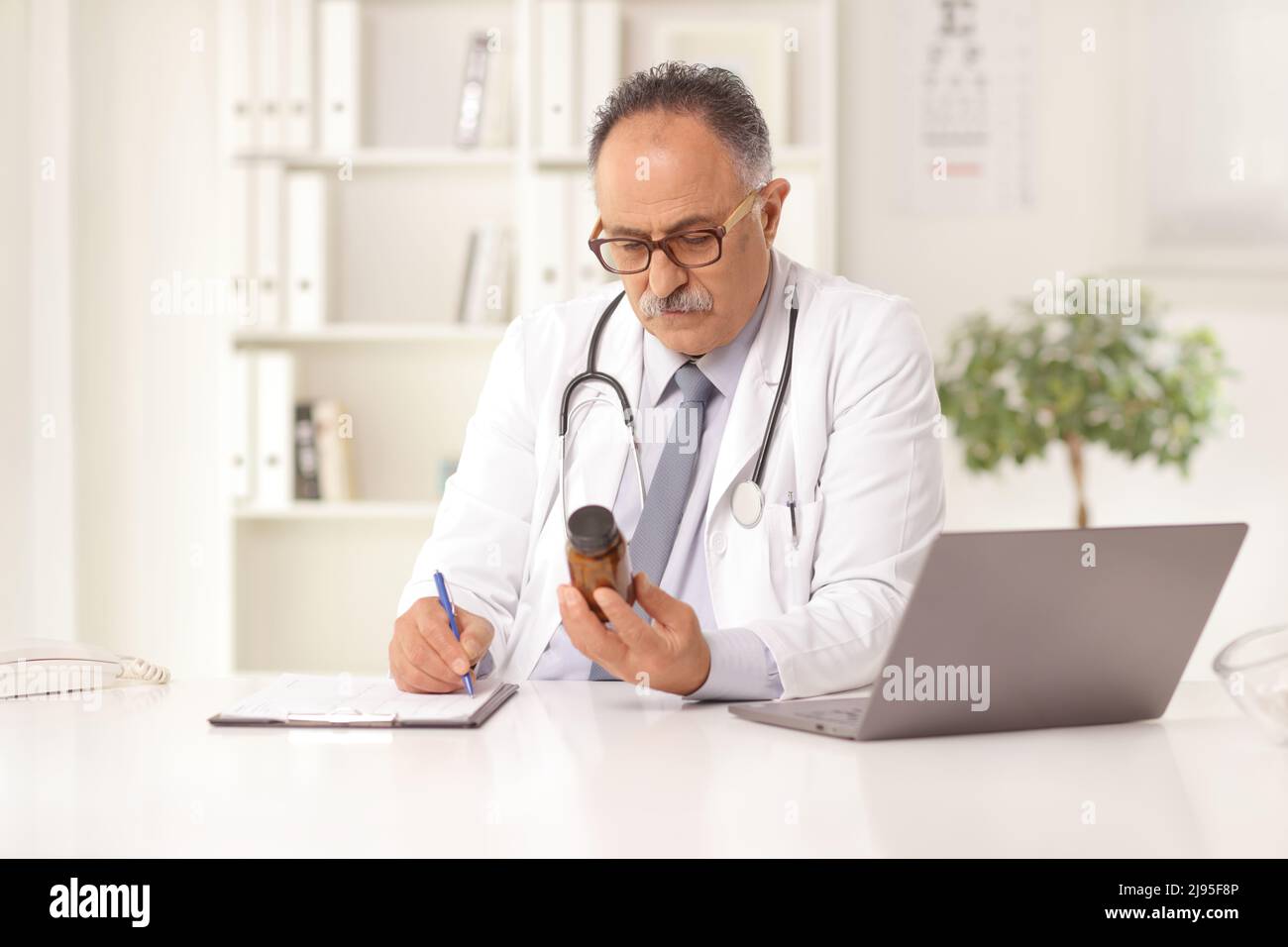 Mature male doctor sitting in an office with a laptop computer on the ...
