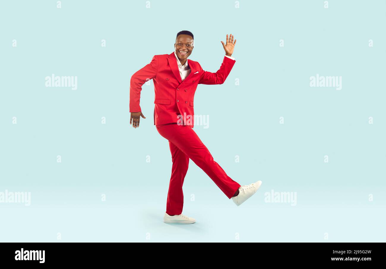 Happy African American man in funky red suit dancing against light blue ...