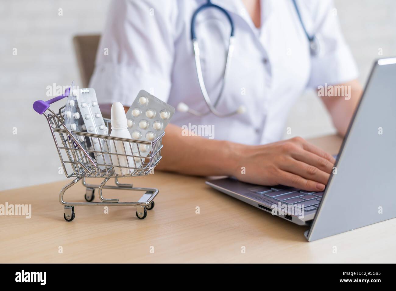 Female doctor working on a laptop. Mini shopping trolley full of pills ...