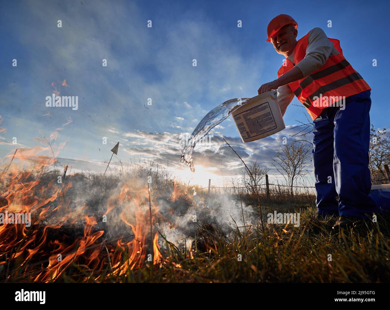Firefighter ecologist extinguishing wildfire in field with evening sky ...