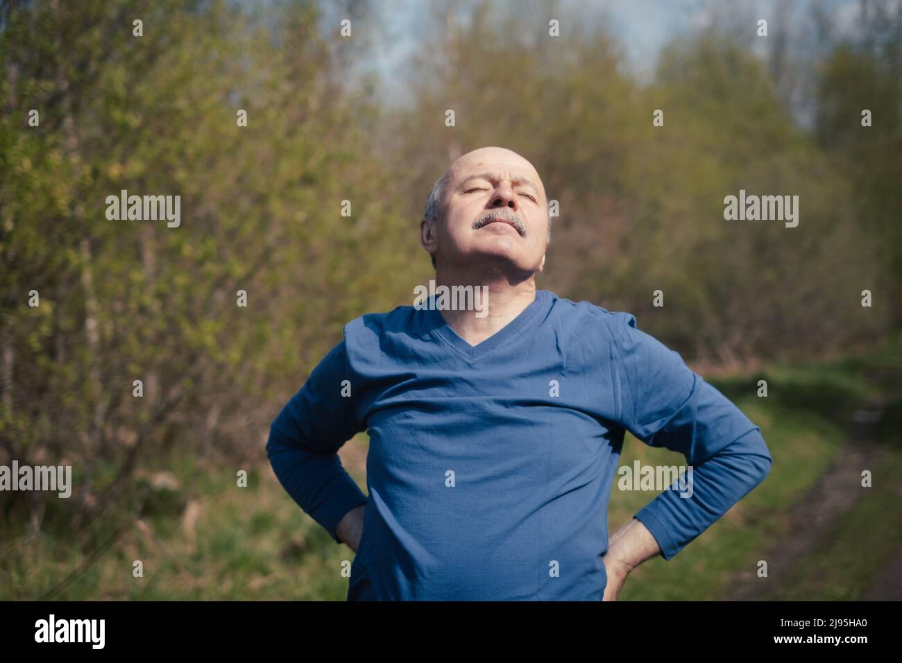 Senior runner with armband doing stretching, breathing fresh air ...