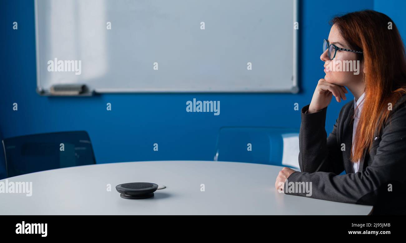 Pensive red-haired office manager in glasses and a suit in an empty ...