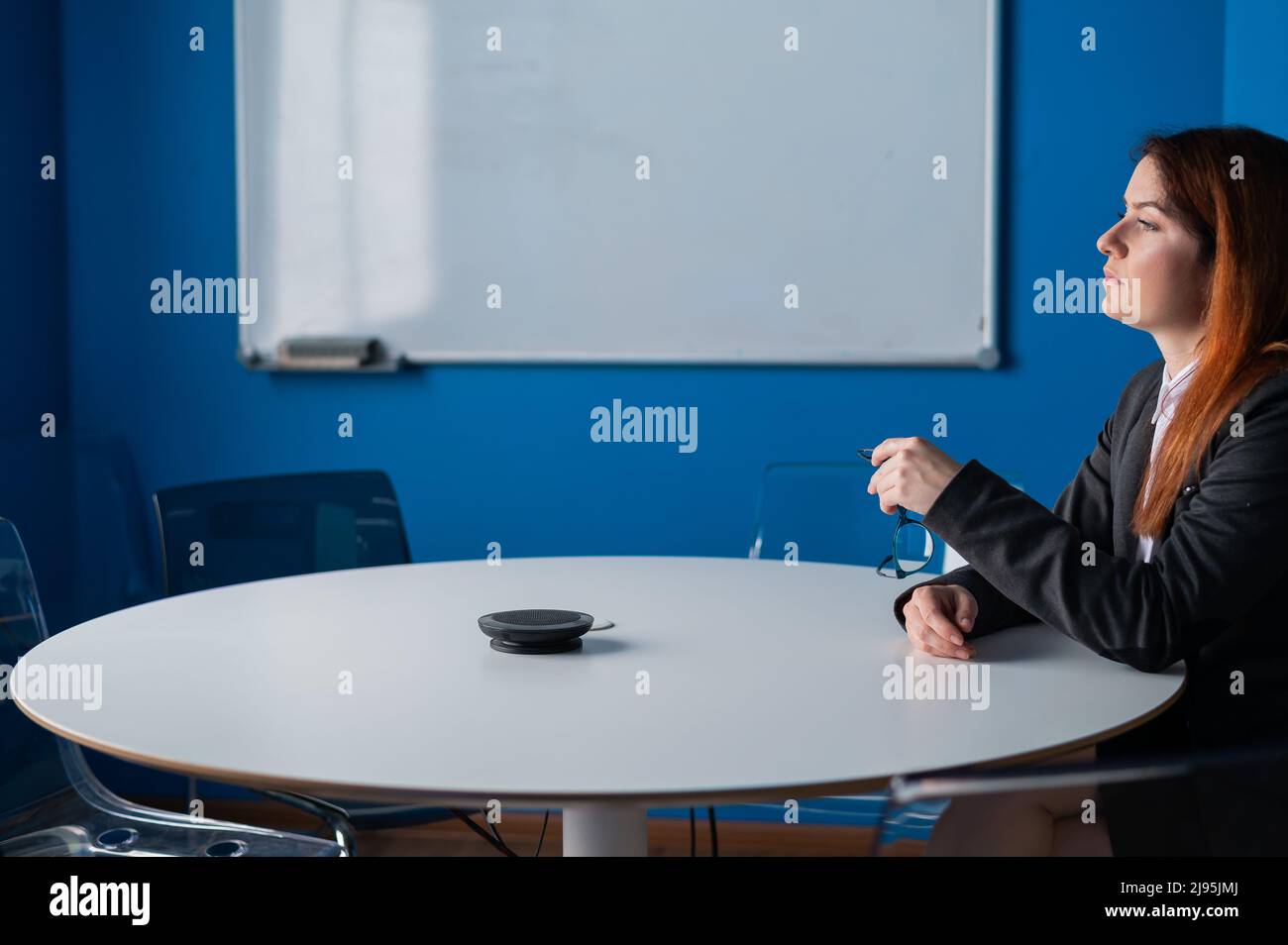 Pensive red-haired office manager in glasses and a suit in an empty ...