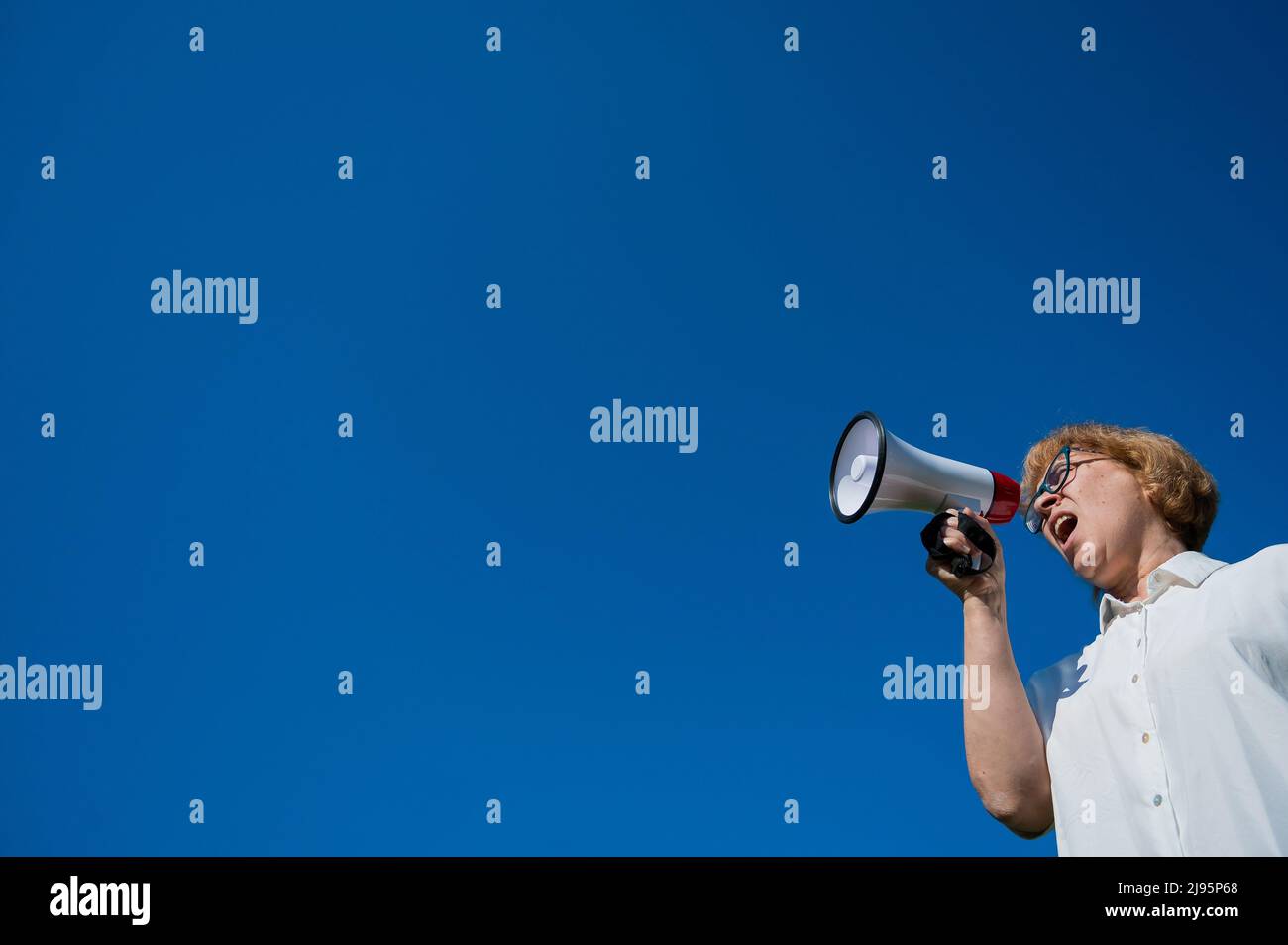 Angry senior woman in glasses shouting into a megaphone on the outside ...