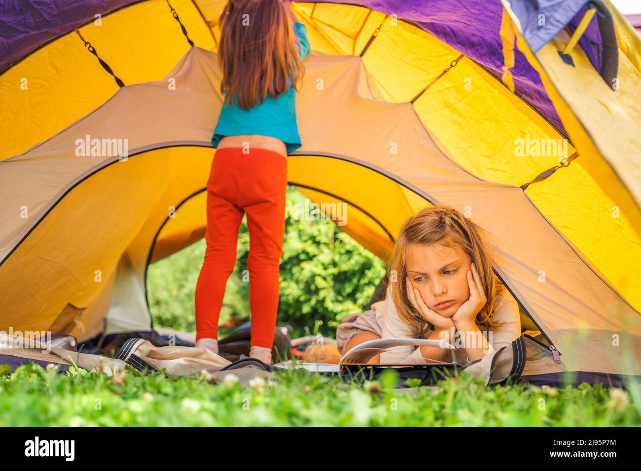 Small children, kids play,read book in orange tourist tent. Family trip ...