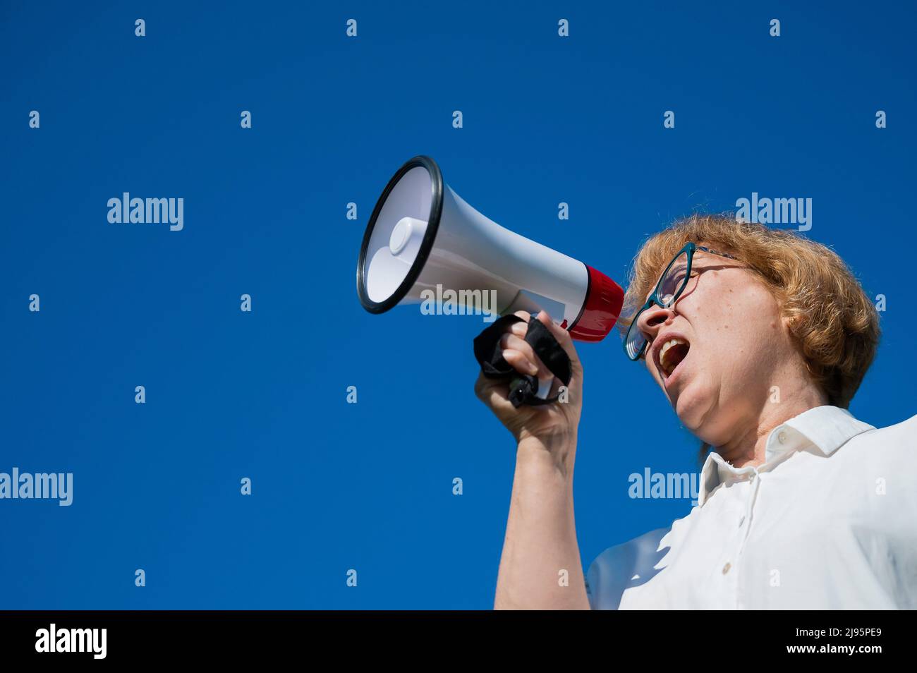 Angry senior woman in glasses shouting into a megaphone on the outside ...