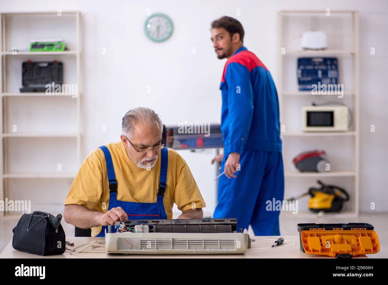 Two repairmen repairing air-conditioner at workshop Stock Photo - Alamy