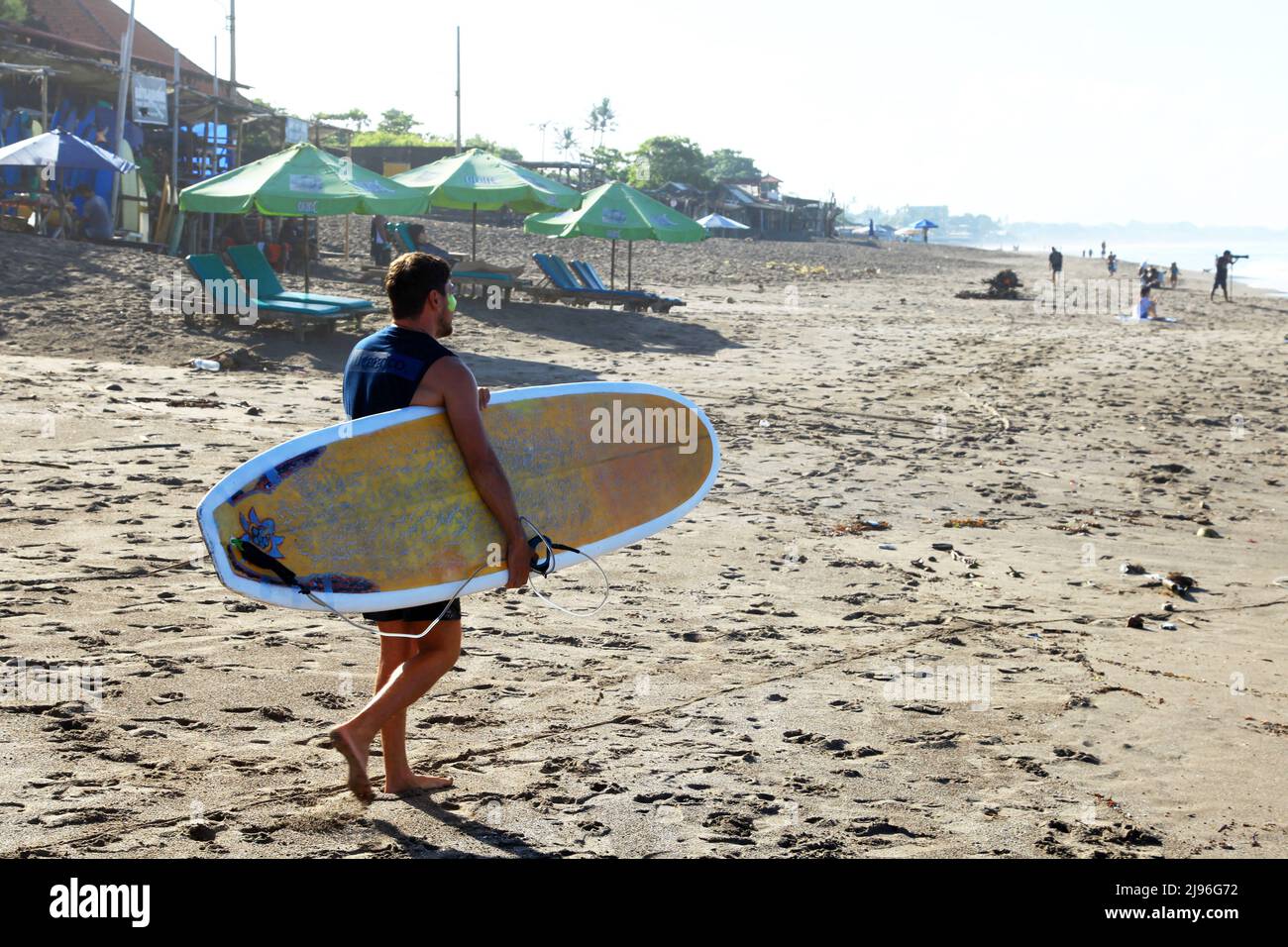 A Caucasian surfer carrying a longboard surfboard towards the sea at ...