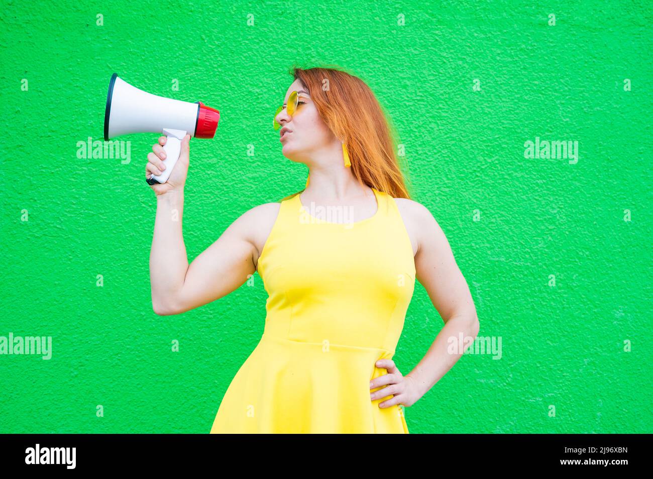 Red-haired woman in sunglasses and a yellow dress holds a megaphone on ...