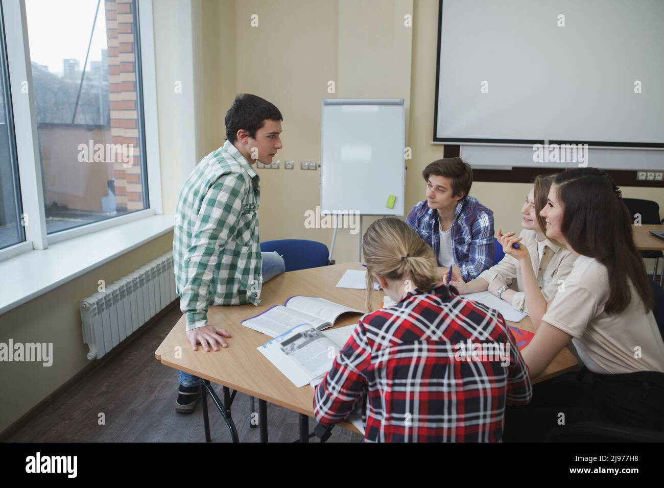Male student sitting on a table, talking to his classmates during class ...