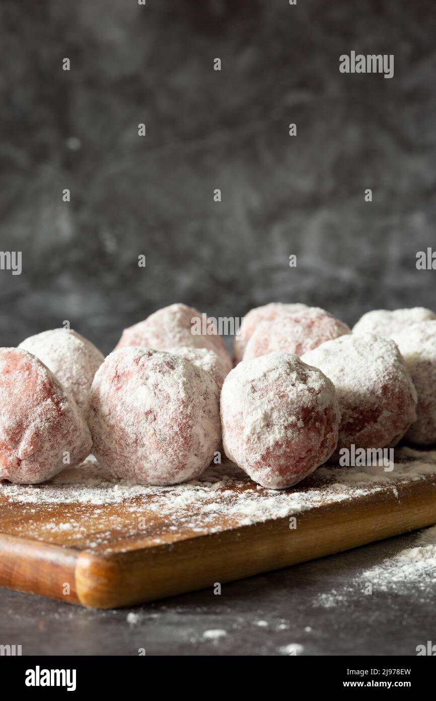 Beef meatball coated in flour on a wooden chopping board. On a black ...