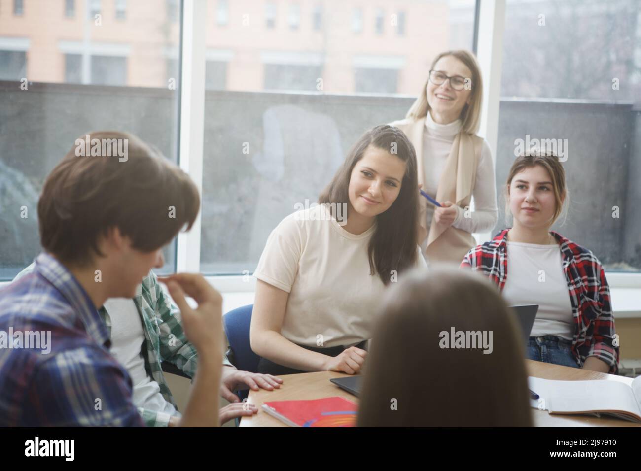 Happy college students and their teacher listening to a classmate ...