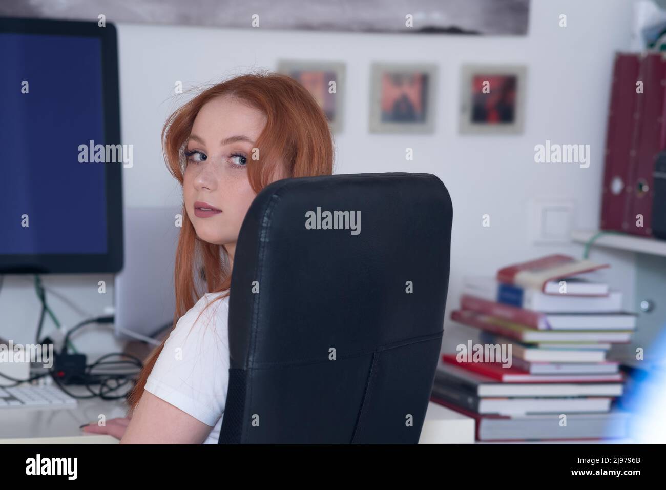young woman sitting at a table in front of a computer monitor turning ...