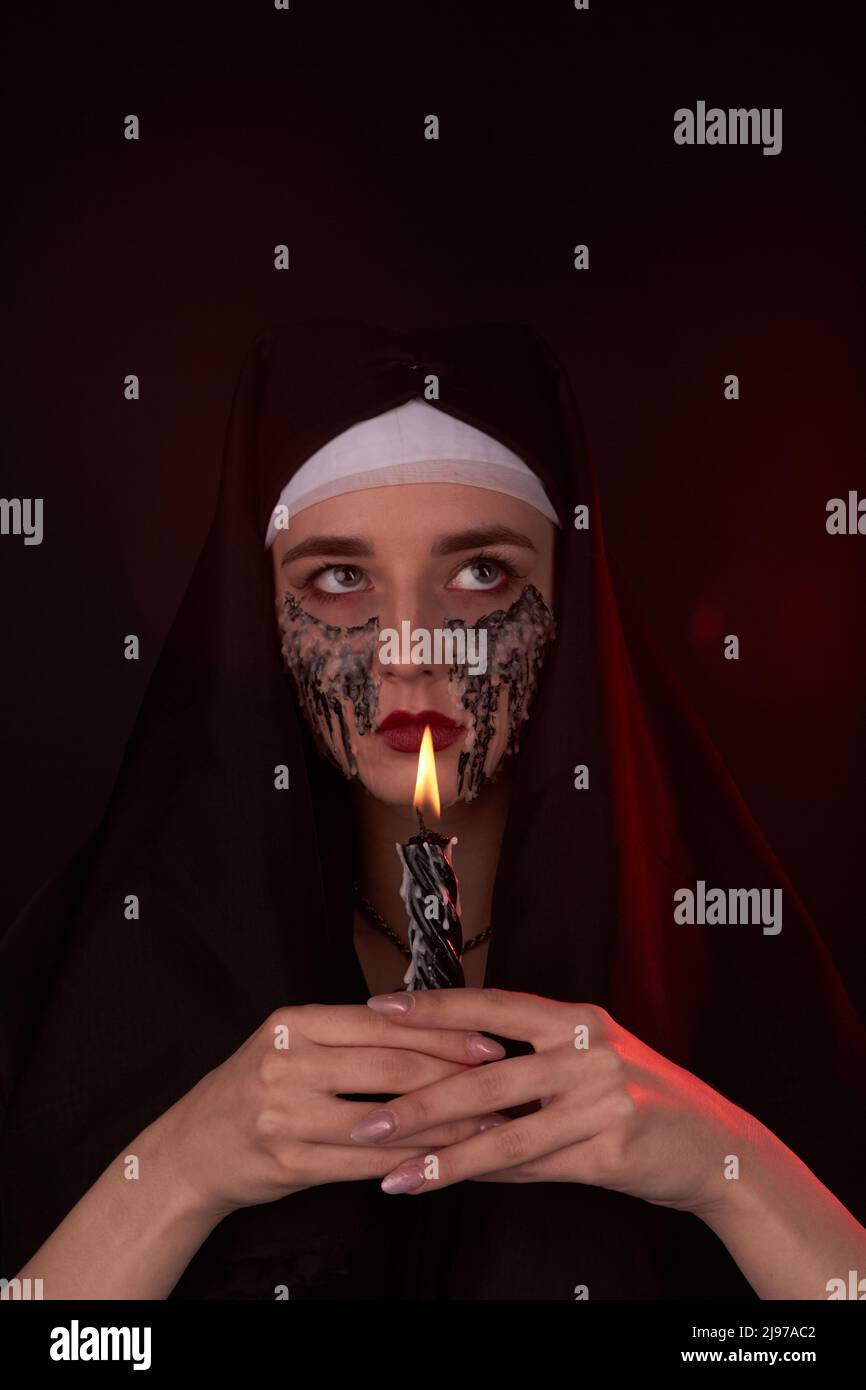 Portrait of a creepy satanic girl holds candle in both hands. Woman ...