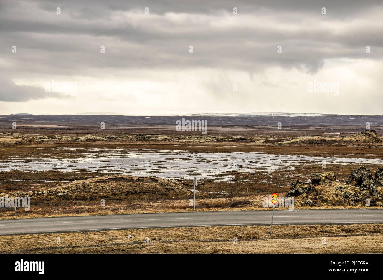 Two lane asphalt road in a desolate landscape with shallow puddles and ...