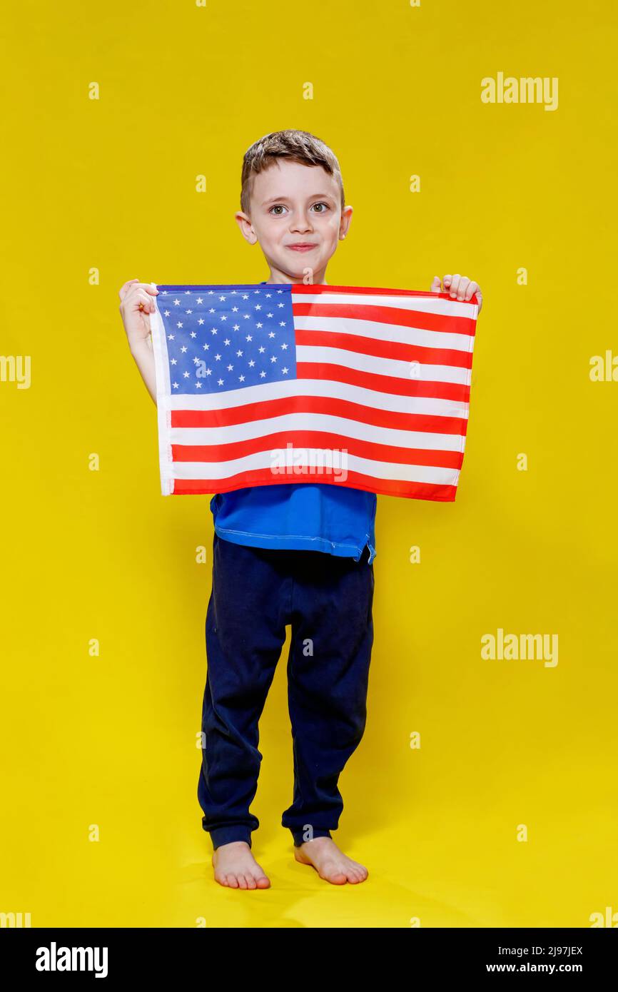 Little smiling boy holding an American flag on a yellow background ...