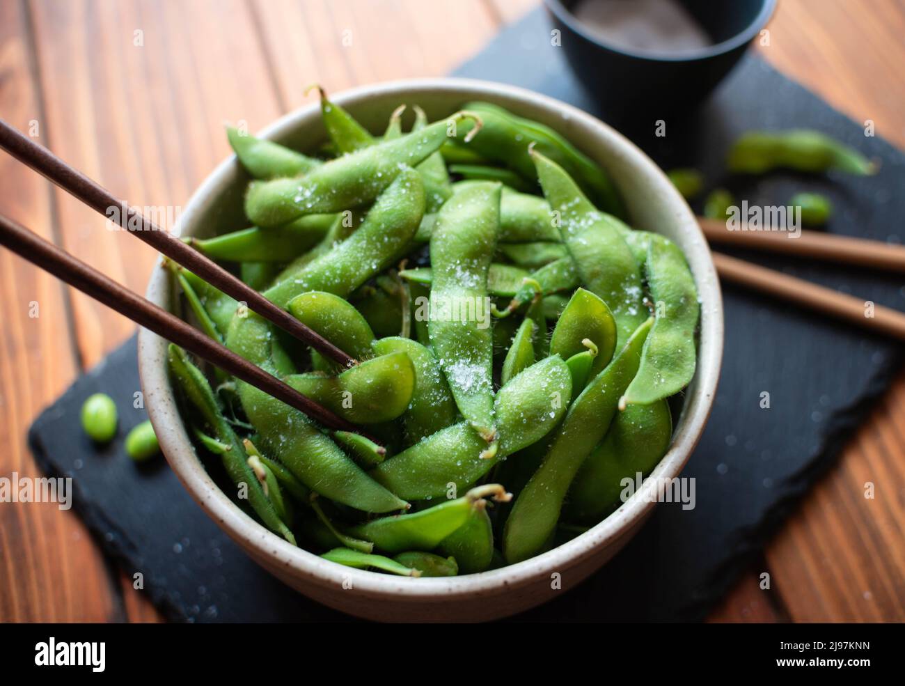 Close-up of steamed edamame sprinkled with sea salt on a dark stone ...