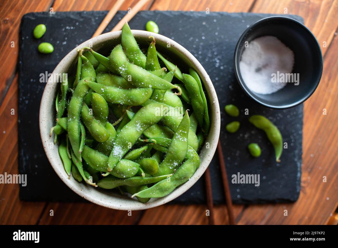 Steamed edamame sprinkled with sea salt on a dark stone board, top view ...