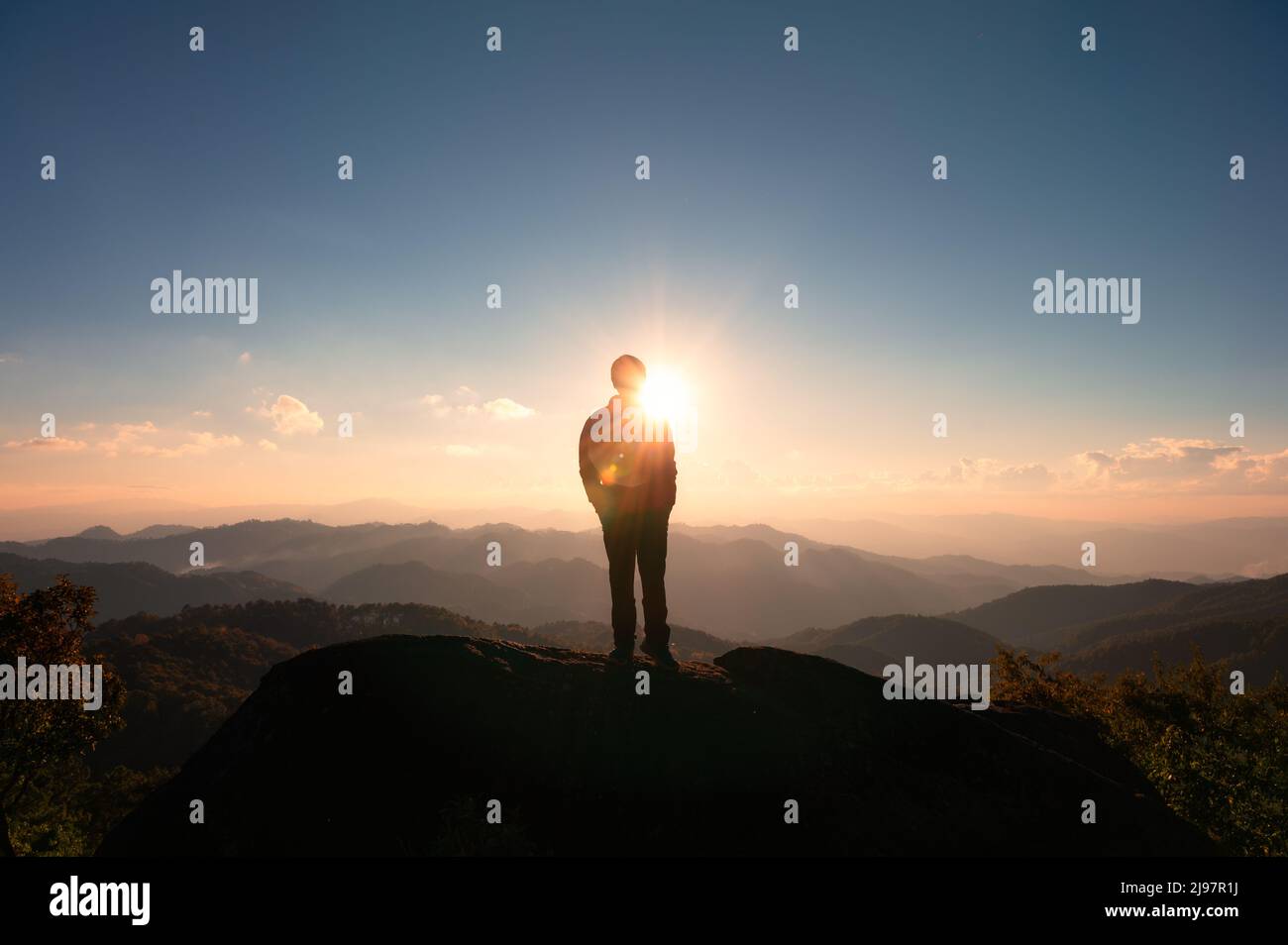 Successful young hiker man standing on top of mountain with the sun in ...