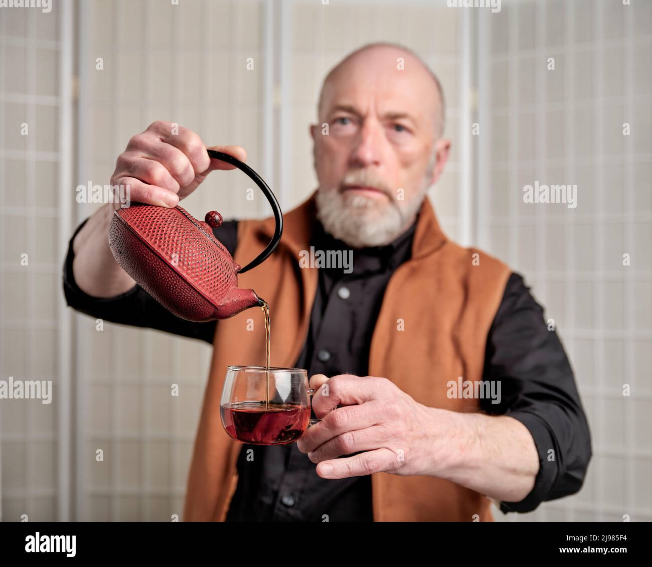 casual portrait of senior man pouring tea from an iron teapot into a ...