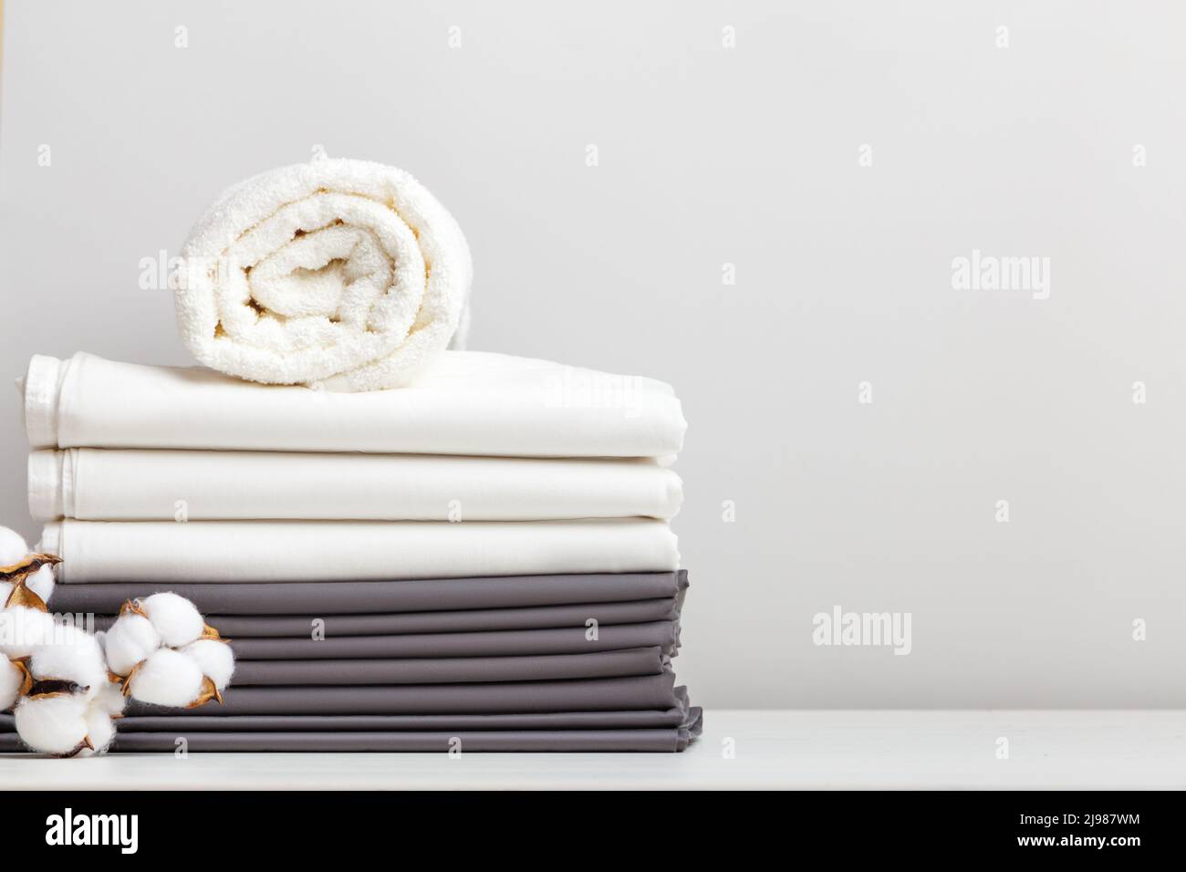 A stack of gray and white bed linens, sheets and a folded roll towel ...
