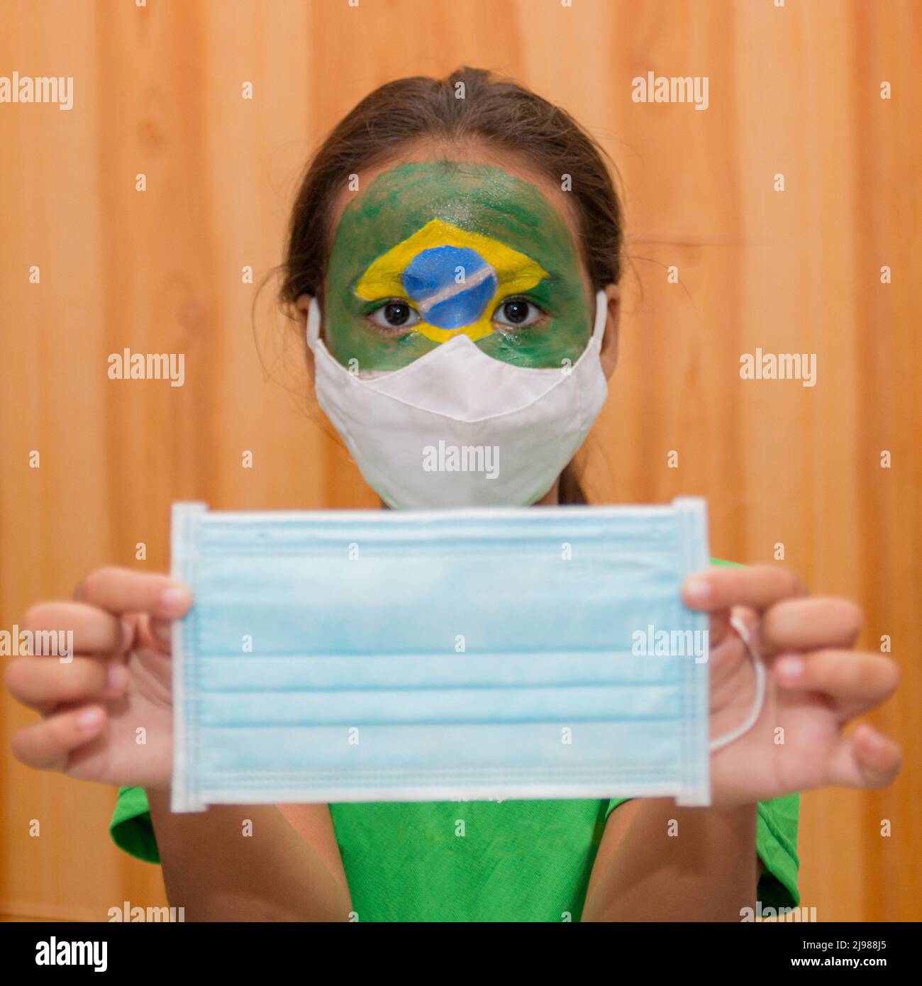 child with mask with face painted with the flag of brazil, holding a ...