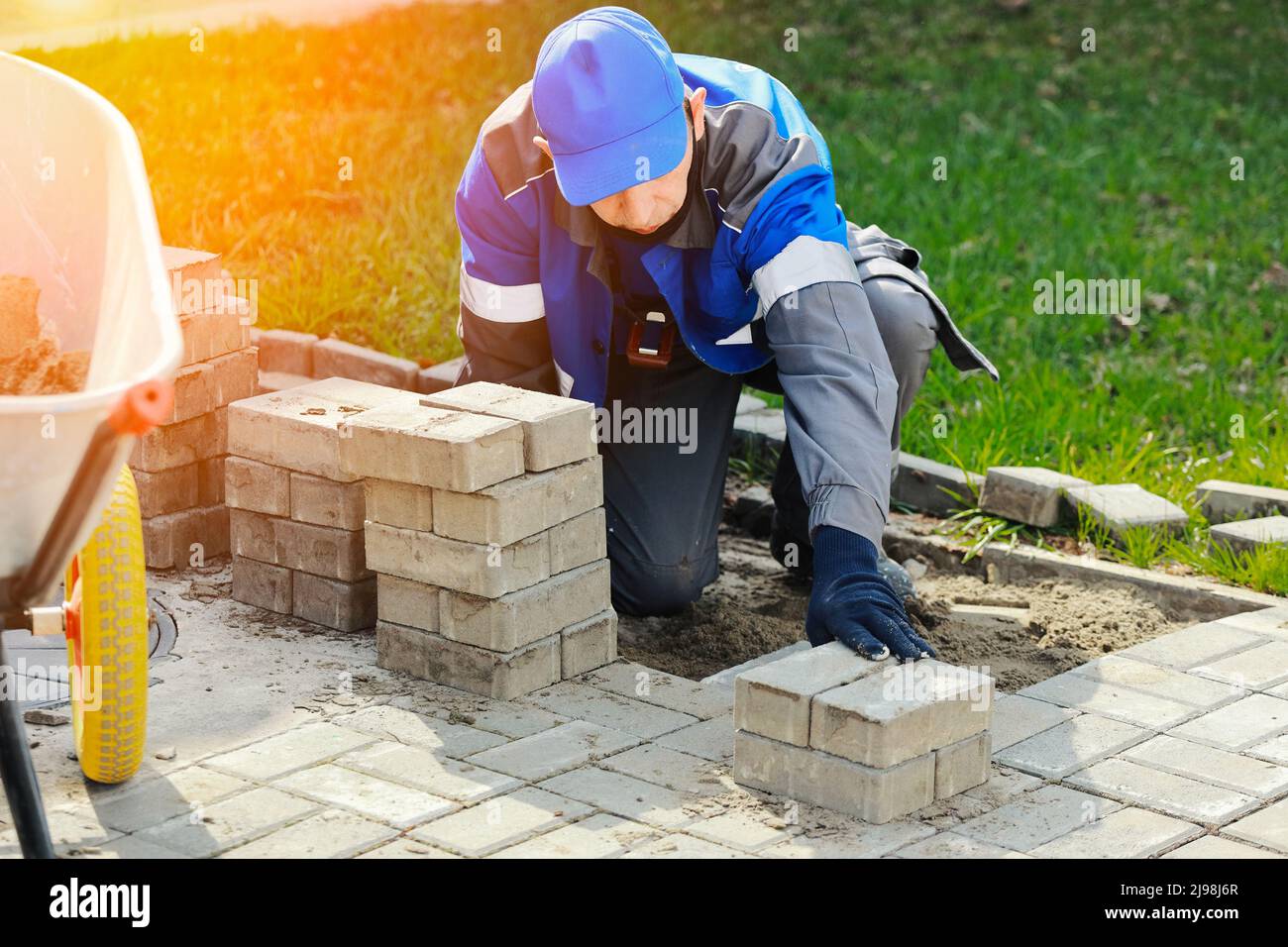 Bricklayer in work clothes sits on sidewalk and lays out paving slabs ...