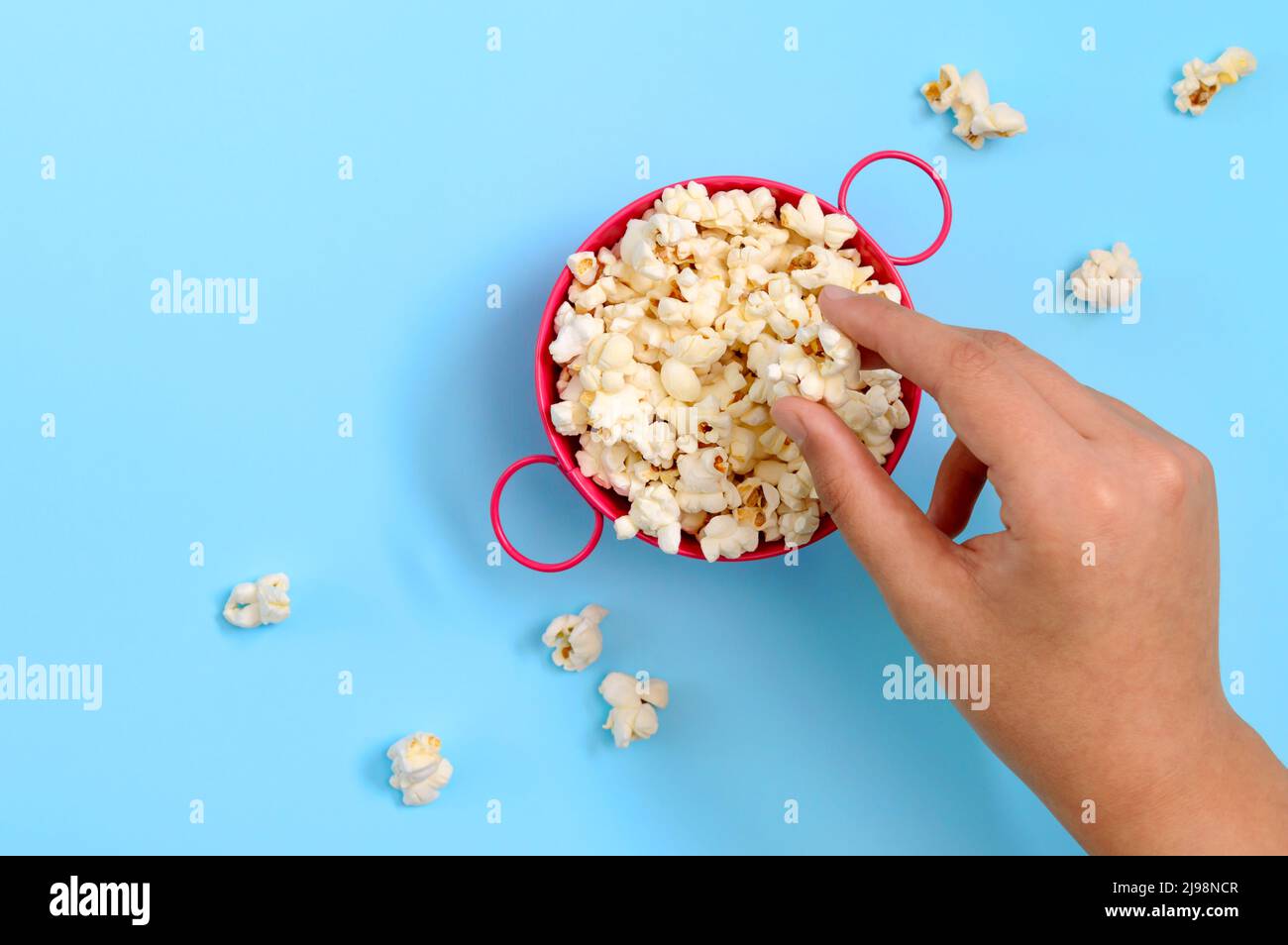 Popcorn, the top view on blue background. Human eating popcorn. Hand ...