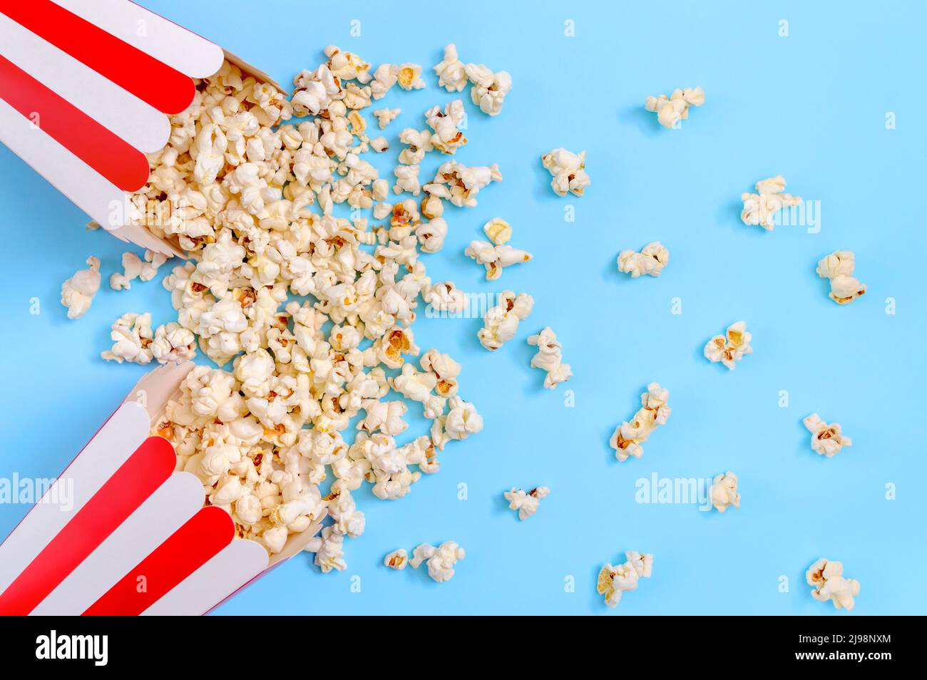 Popcorn spills out of the paper striped cups on a blue background ...