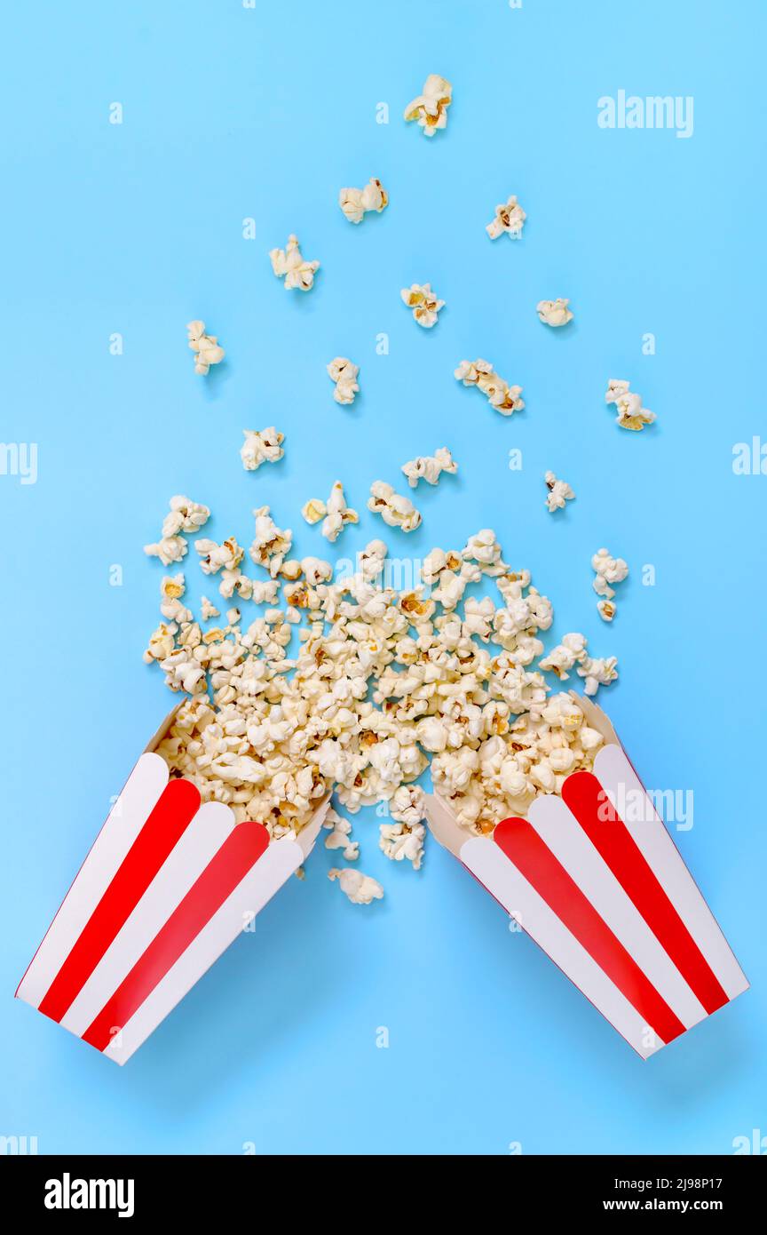 Popcorn spills out of the paper striped cups on a blue background. A ...