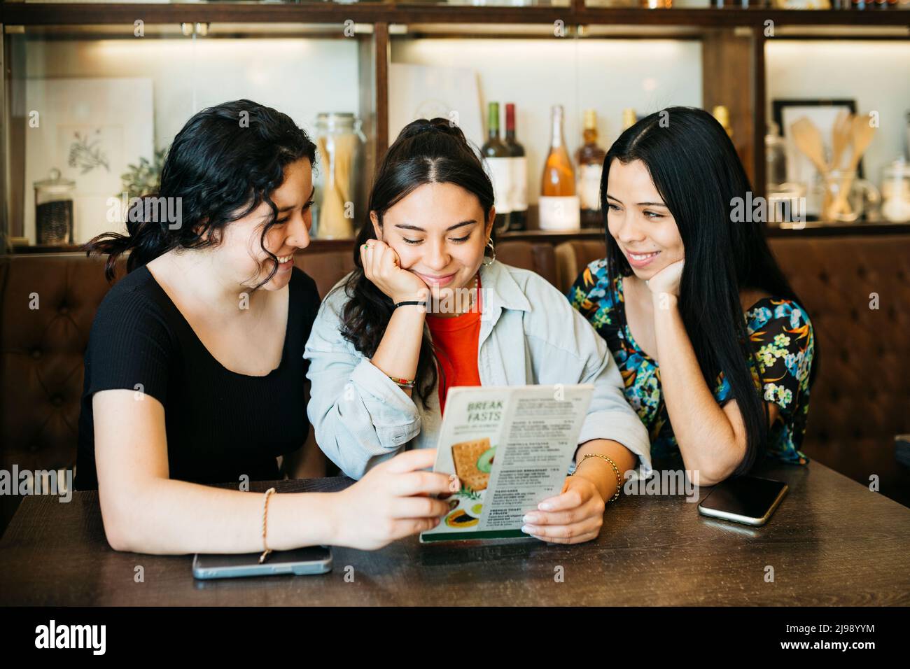 Three young women looking at a menu in a restaurant Stock Photo - Alamy