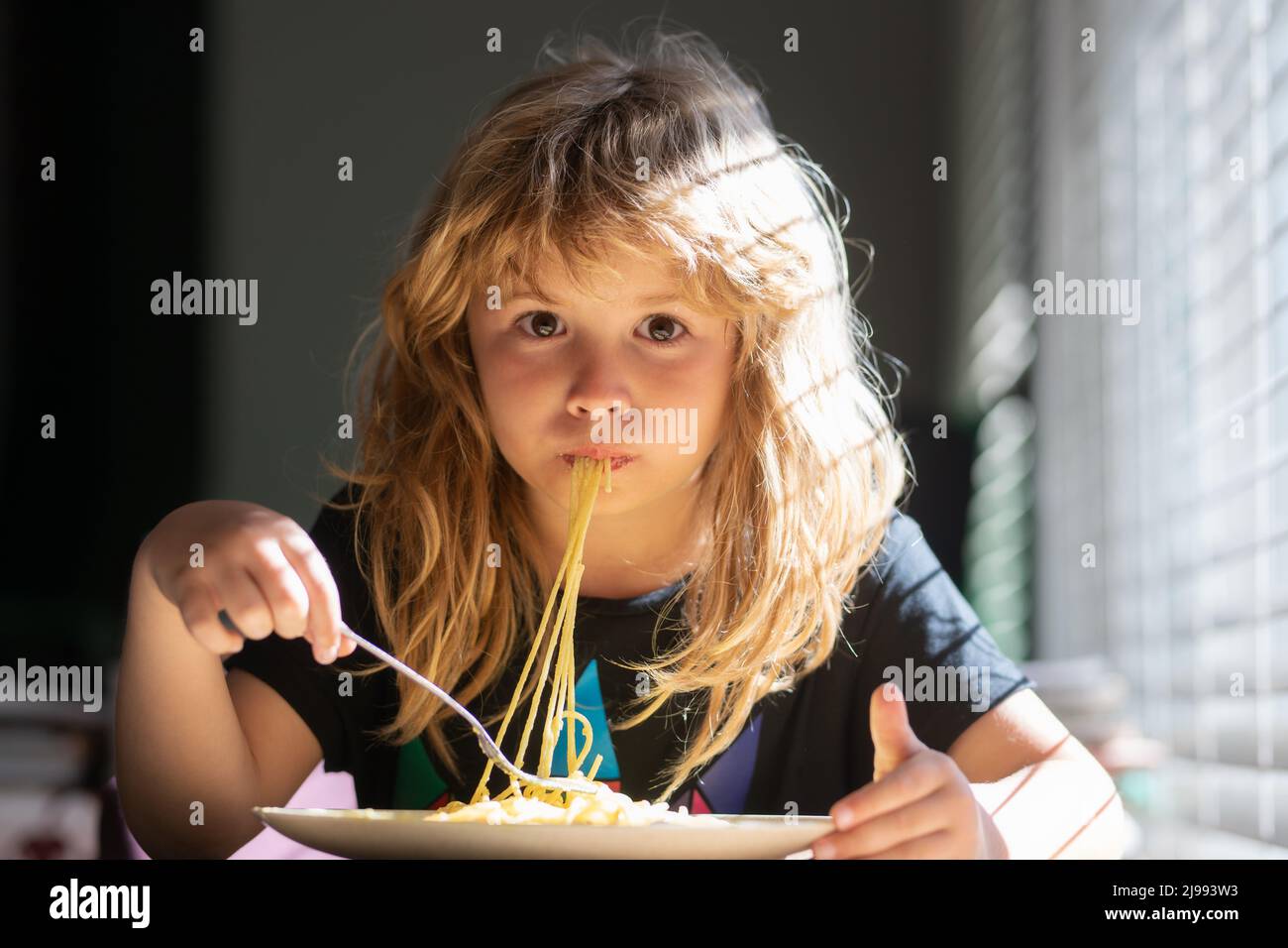 Cute little kid eating spaghetti pasta at home. Close up portrait of ...
