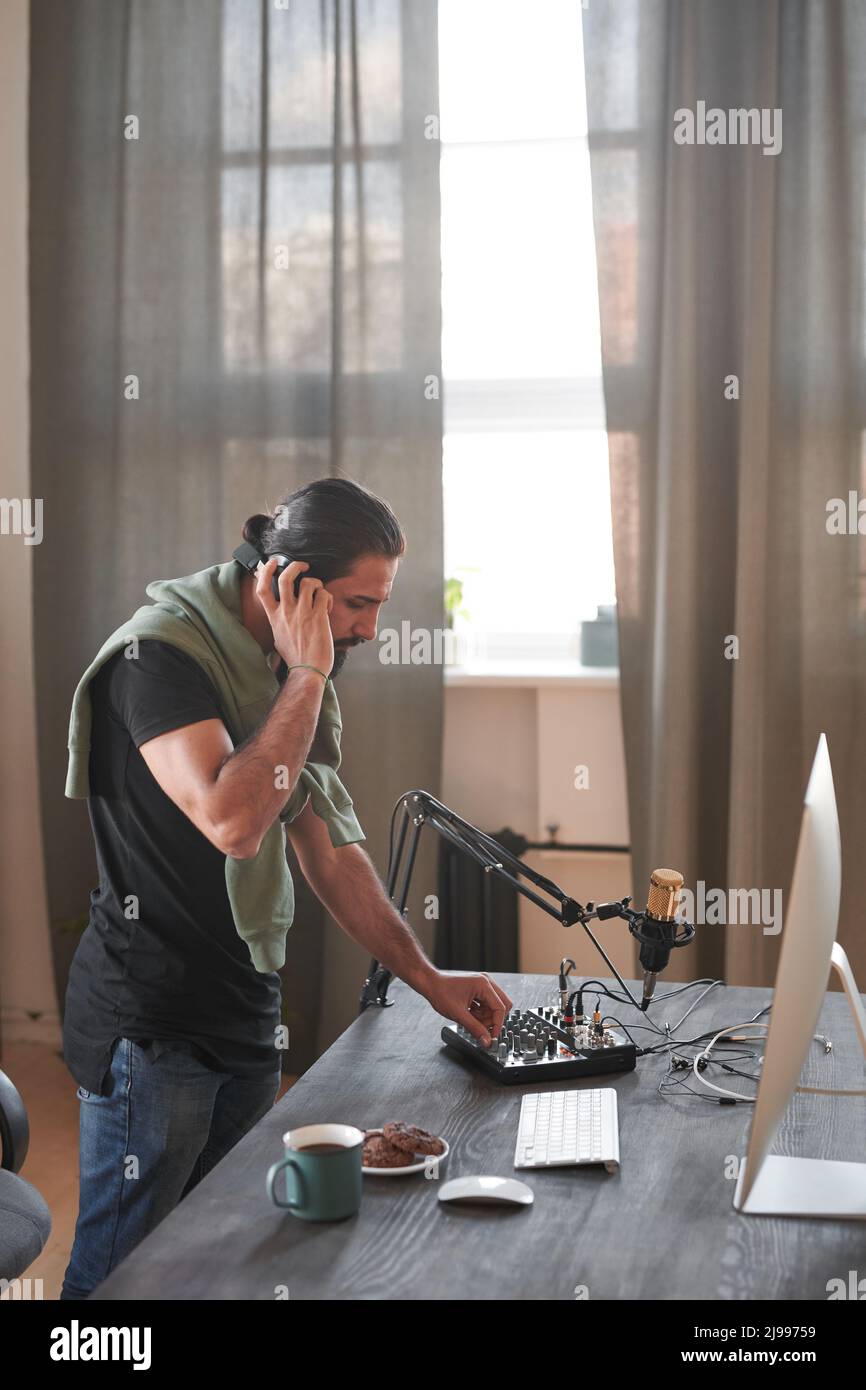 Vertical long shot of young bearded influencer adjusting sound in home ...