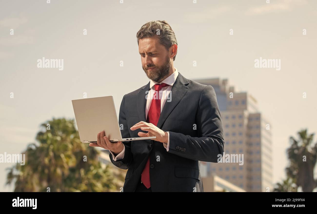 confident man in elegant suit checking email on pc outside, agile ...