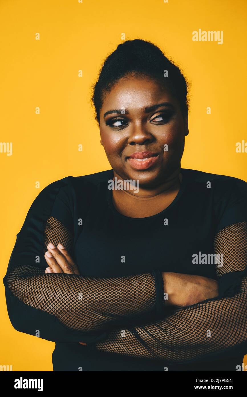 portrait of a beautiful black woman smiling with crossed arms on yellow ...