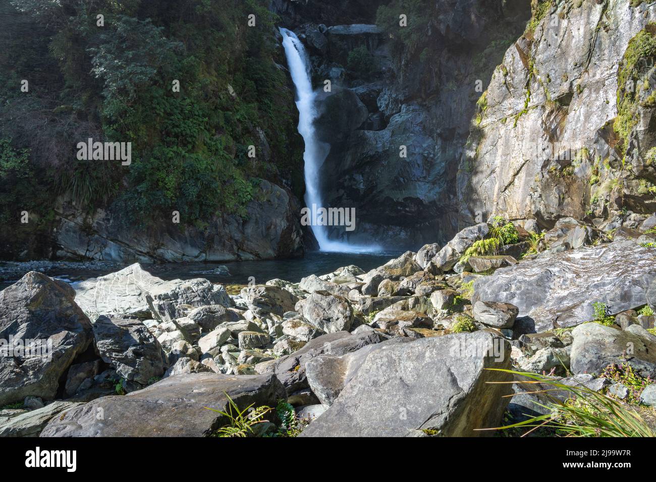 Tall waterfall drops from high point to pool surrounded by rocky ...