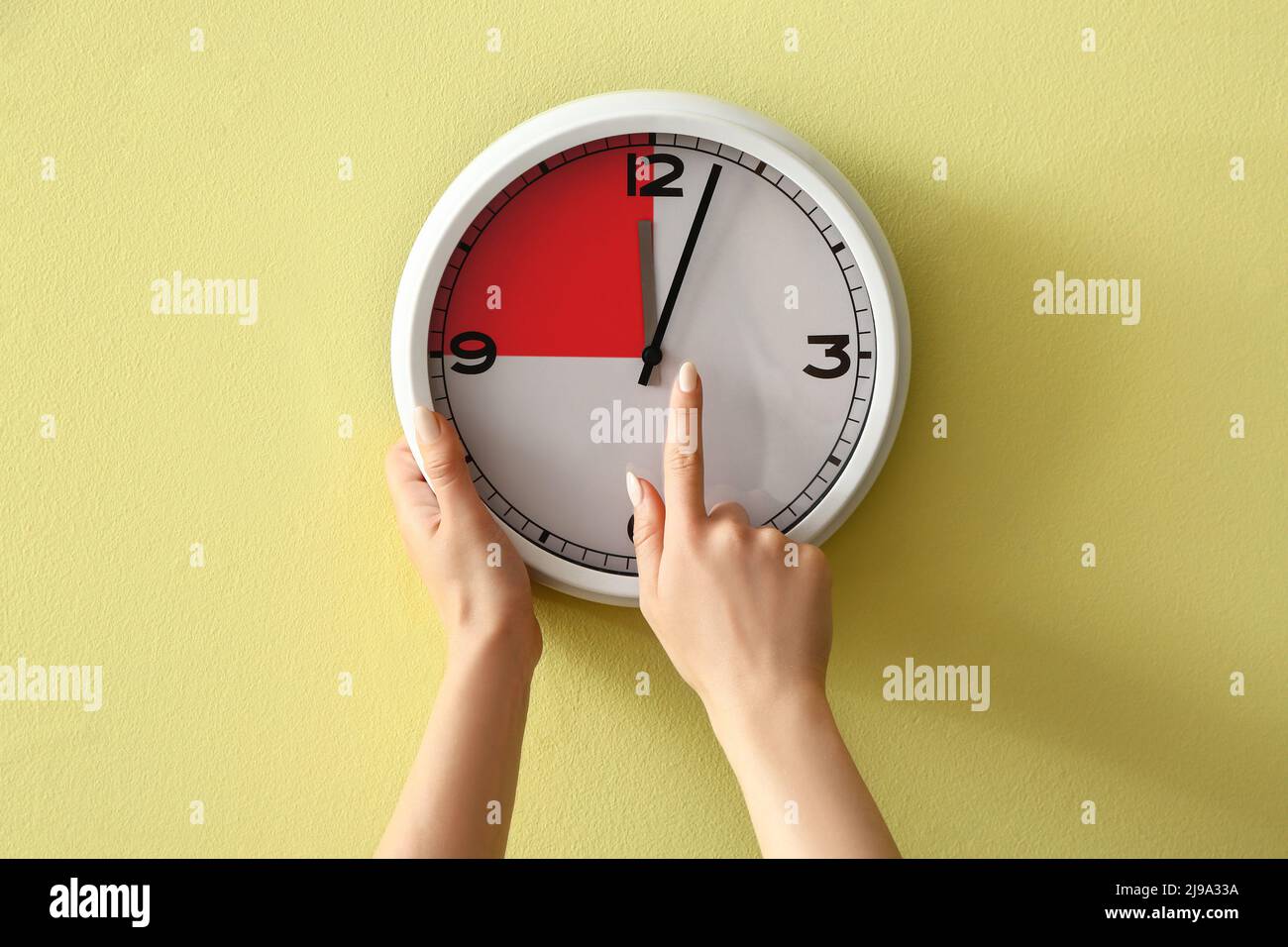 Female hands touching clock on yellow wall Stock Photo - Alamy