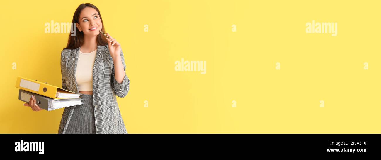 Thoughtful young woman holding folders on yellow background with space ...