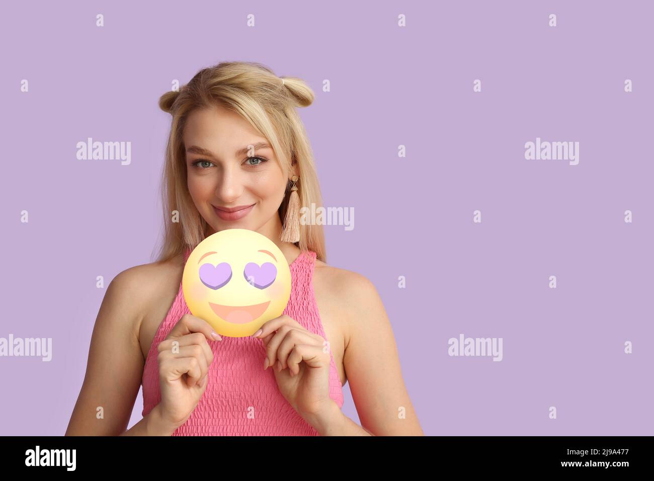 Pretty young woman holding happy emoticon with heart-shaped eyes on ...