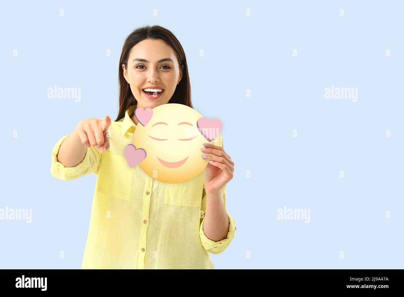 Beautiful young woman holding smiling emoticon with hearts on light ...