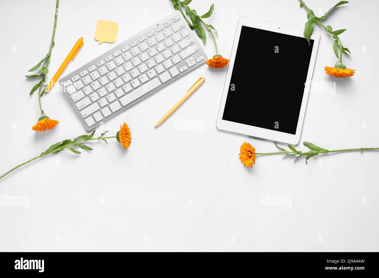 Tablet with computer keyboard, pens, sticky note and flowers on white ...