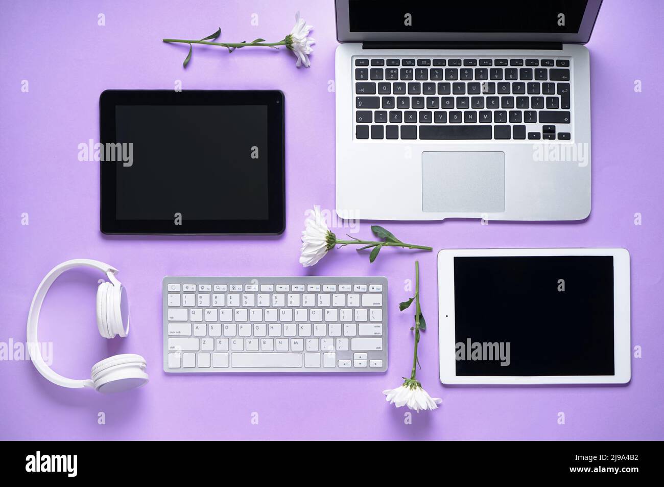 Laptop with tablet computer, keyboard, headphones and flowers on lilac ...