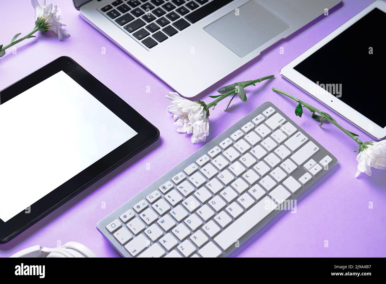 Laptop with tablet computer, keyboard and flowers on lilac background ...